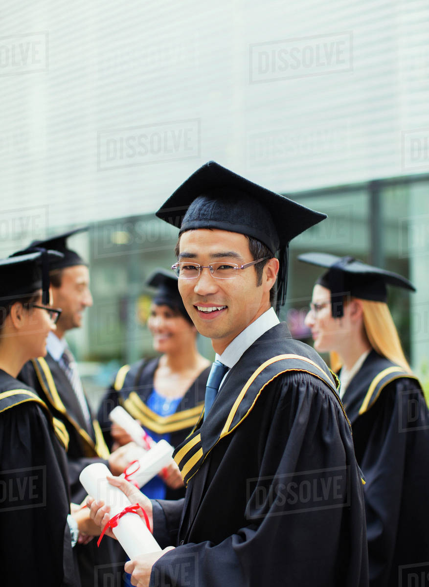 Student in cap and gown standing with friends - Stock Photo - Dissolve