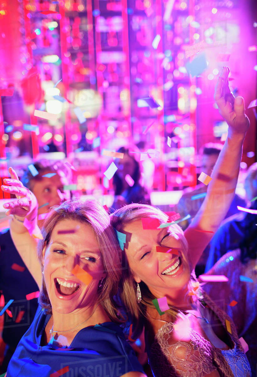Confetti falling on two women dancing back to back in nightclub ...