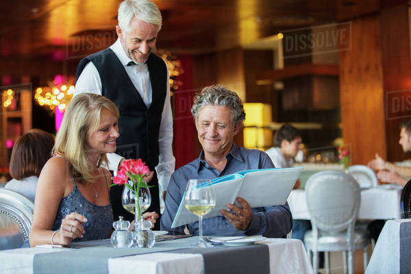Man ordering meal at fancy restaurant table, waiter standing behind ...