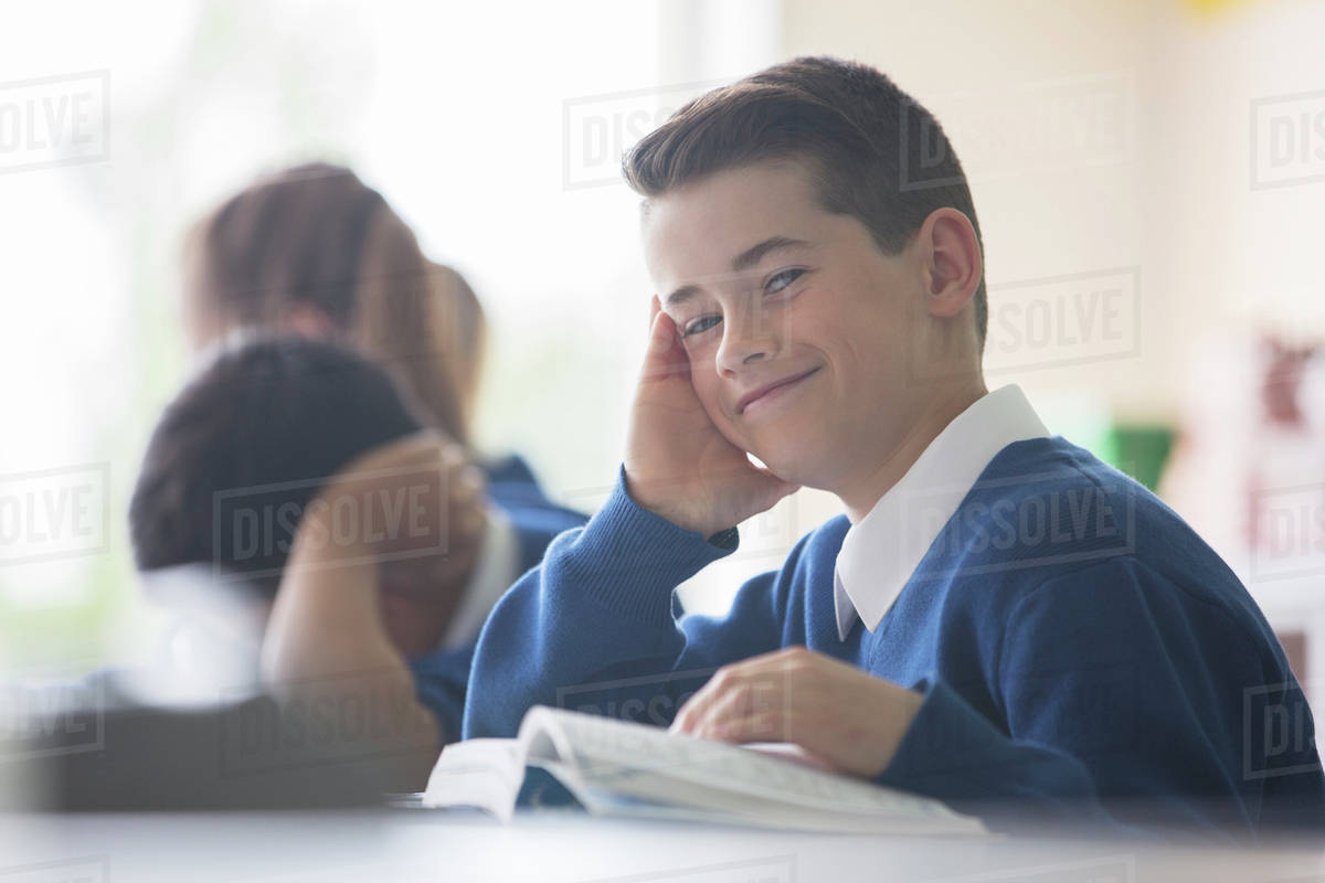 Portrait of smiling elementary school boy sitting at desk in classroom ...