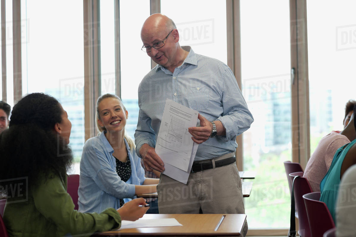 Teacher talking with students during lecture in sunlit classroom ...