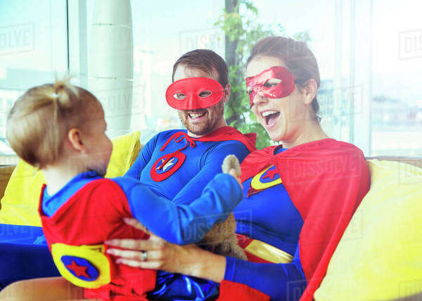 Superhero parents playing with daughter on living room sofa - Stock ...