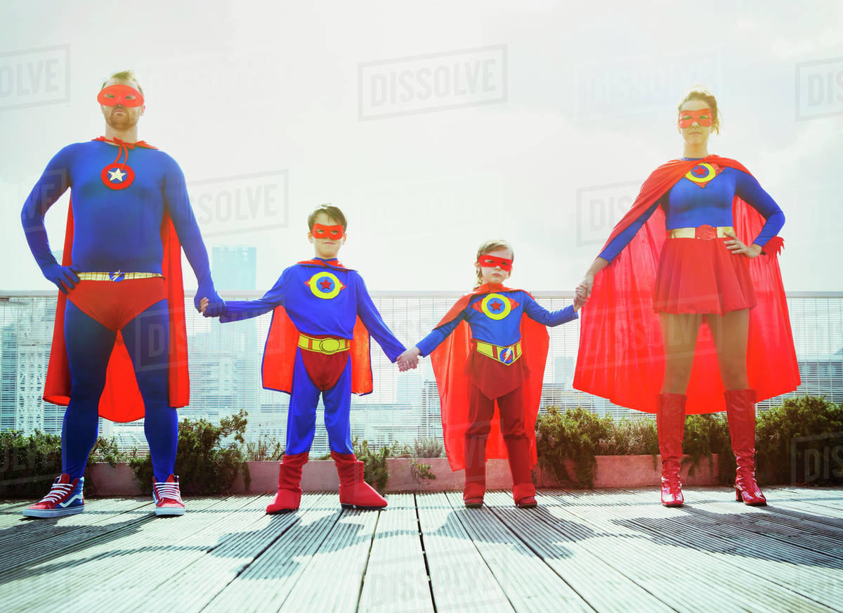 Superhero family holding hands on city rooftop - Stock Photo - Dissolve