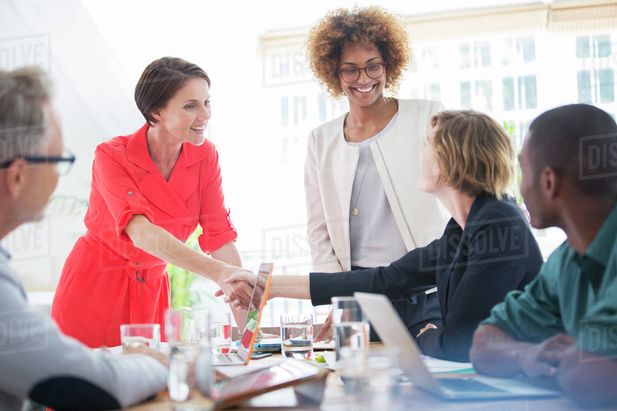 Office workers shaking hands at desk - Royalty-free Stock Photo | Dissolve