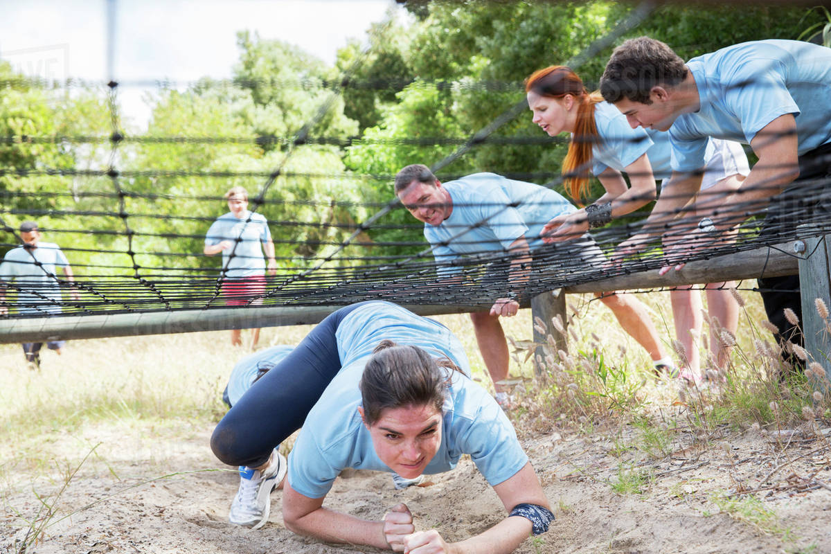 Determined woman crawling under net on boot camp obstacle course ...