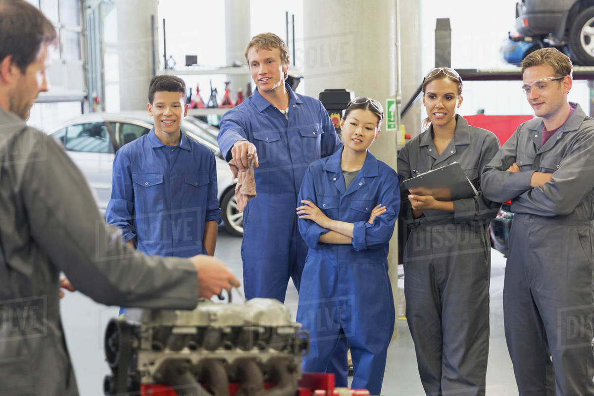 Mechanic and students discussing car engine in auto repair shop ...