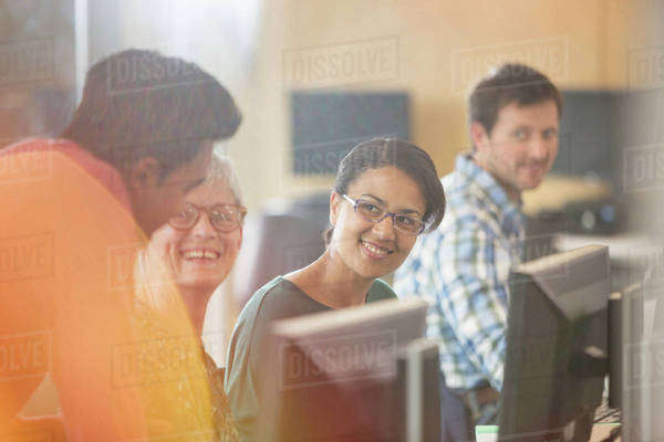 Smiling students talking at computers in adult education classroom ...