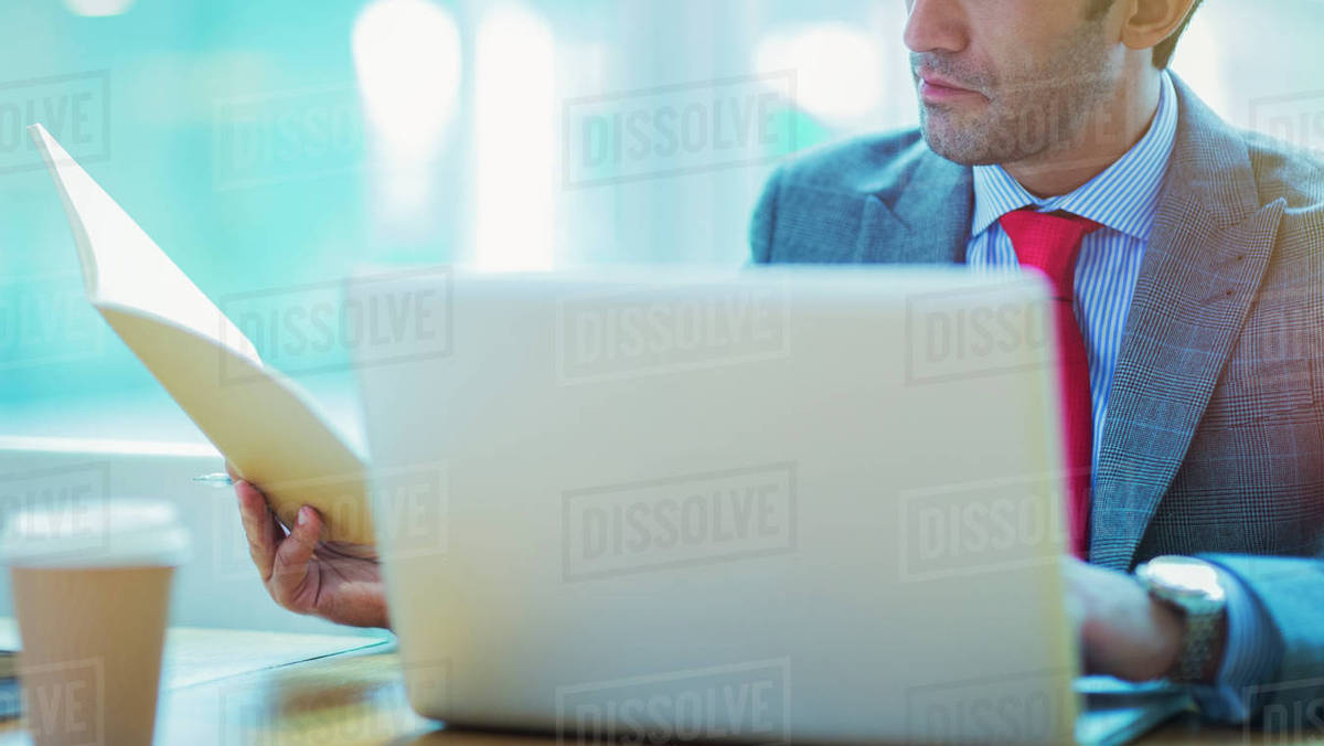 Focused businessman reviewing paperwork at laptop in office - Stock ... Focused businessman reviewing paperwork at laptop in office - Stock ...