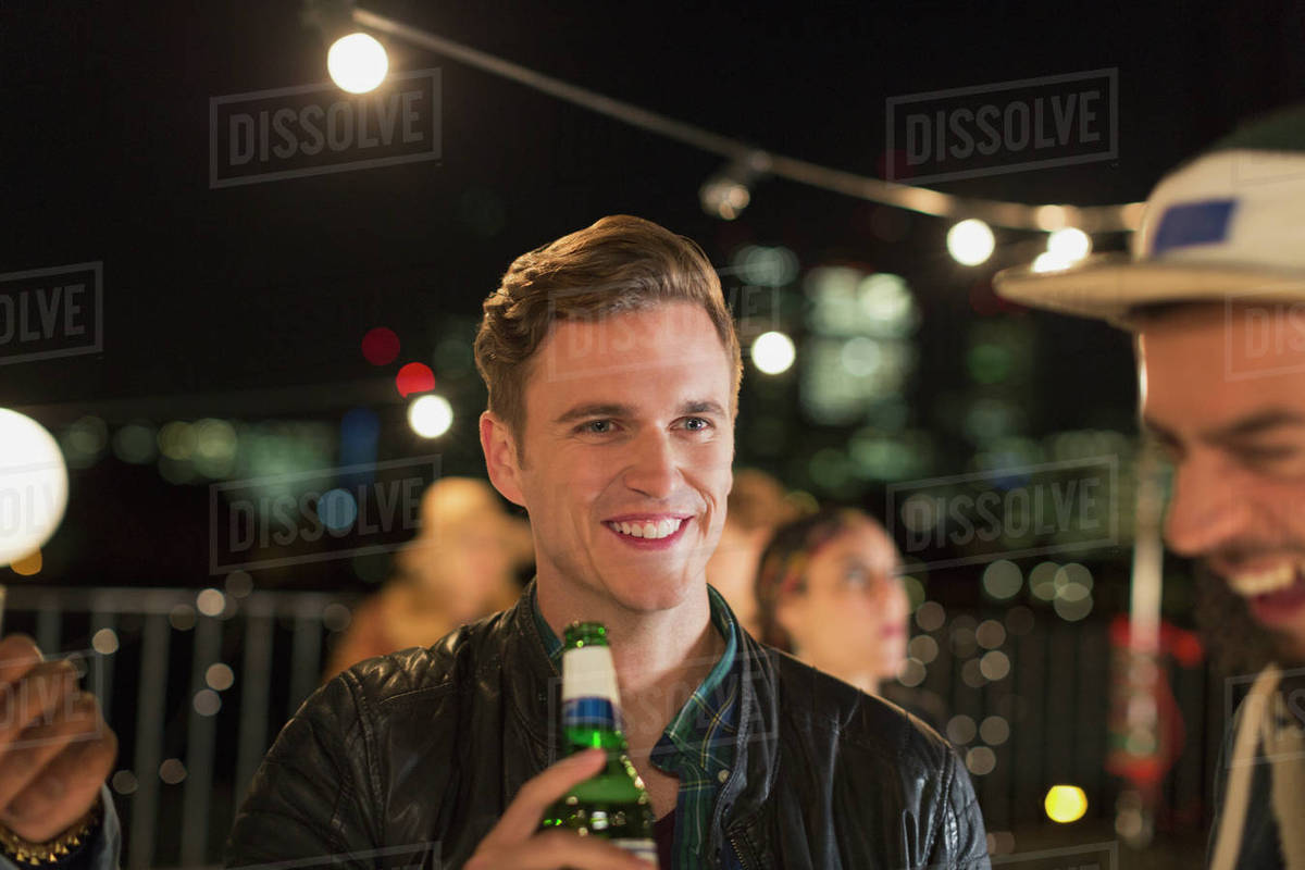 Smiling young man drinking beer at rooftop party - Royalty-free Stock ...