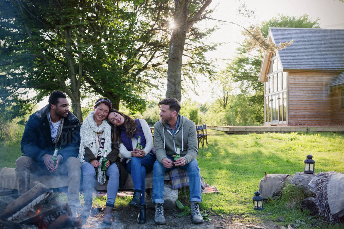 Friends drinking beer relaxing at campfire outside cabin - Stock Photo ...