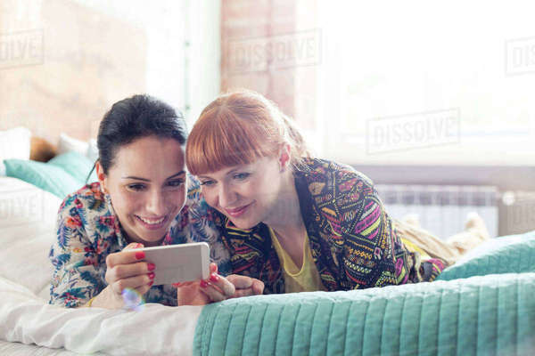 Women using cell phone laying on bed - Royalty-free Stock Photo | Dissolve