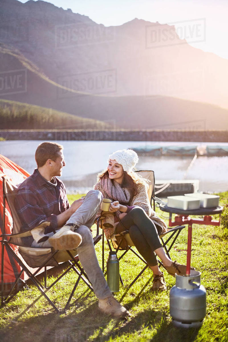 Young couple camping, drinking coffee at sunny lakeside campsite ...