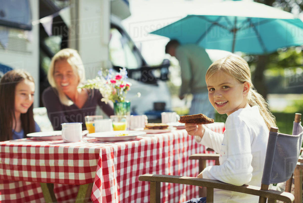 Portrait smiling girl eating breakfast with family outside sunny motor ...