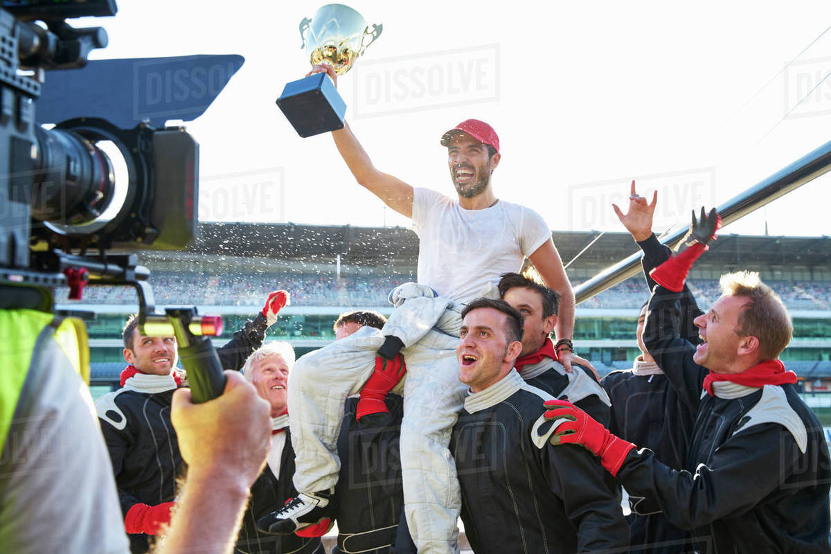 Racing team celebrating victory carrying race car driver with trophy on ...