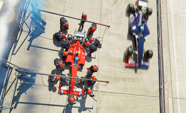 Overhead pit crew replacing tires on formula one race car in pit lane ...