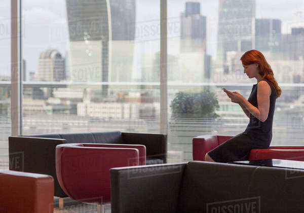 Businesswoman texting with cell phone in urban lounge with city view ...