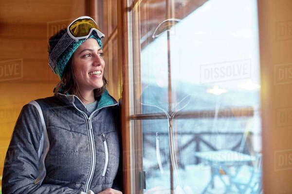Smiling female skier looking out cabin window - Stock Photo - Dissolve