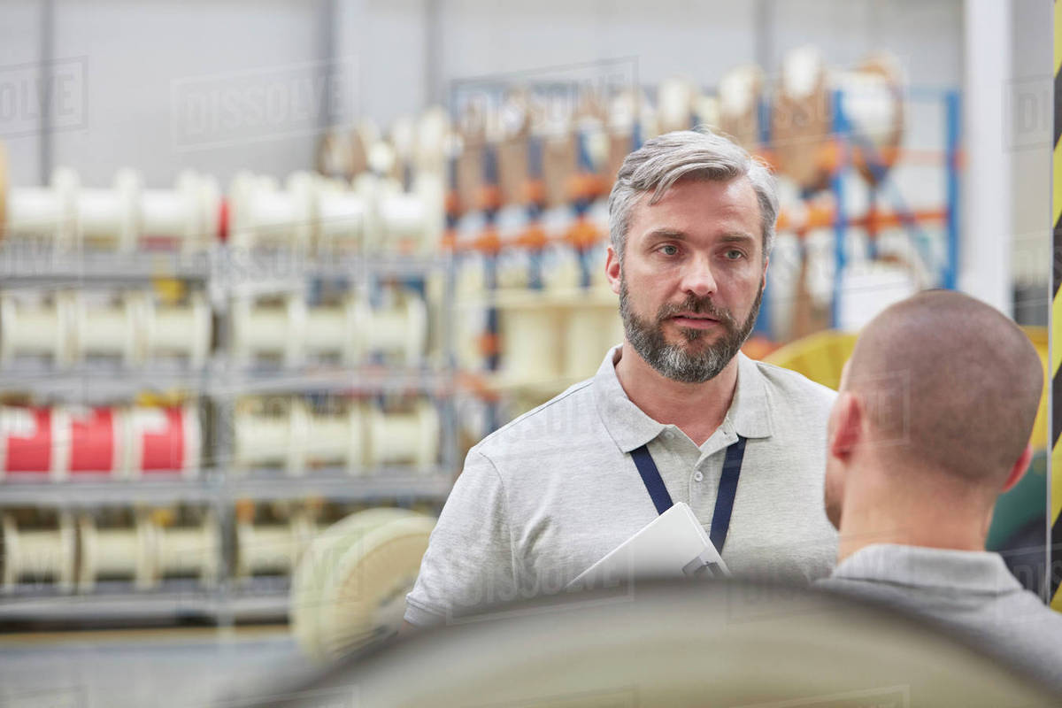 Serious male supervisor listening to worker in fiber optics factory ...