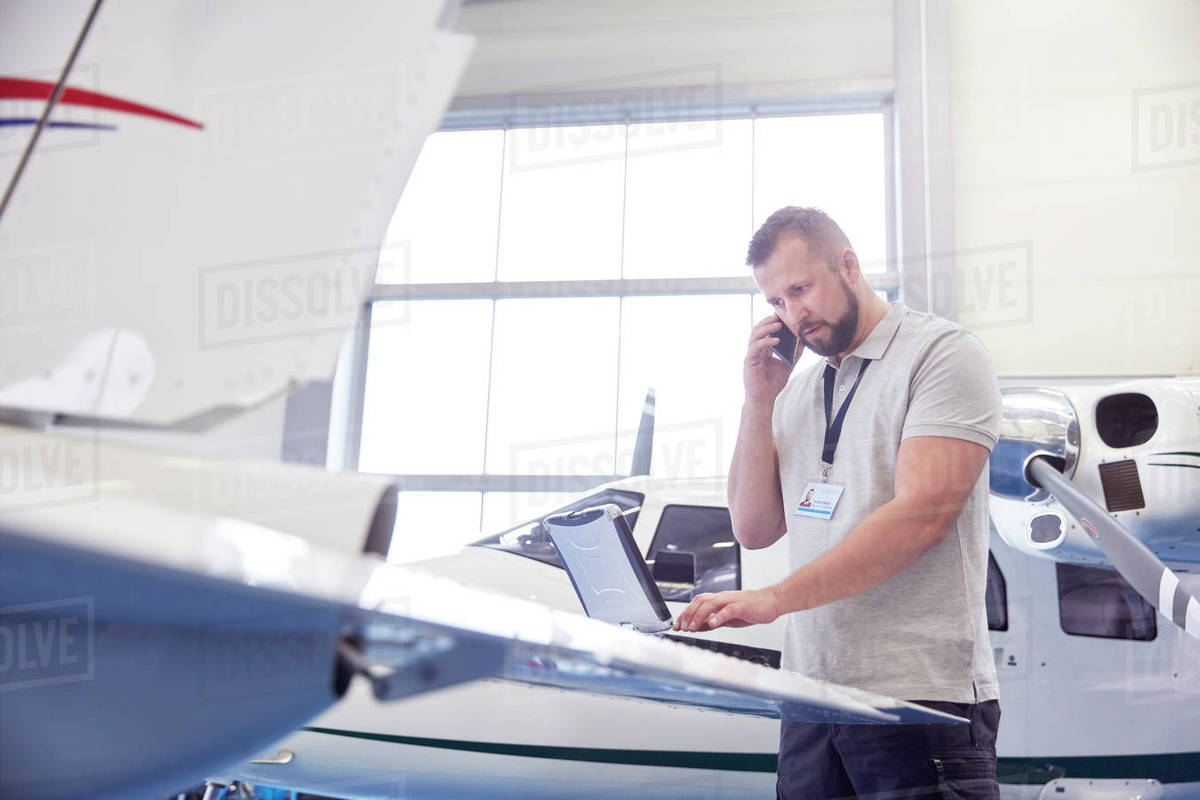 Male airplane mechanic talking on cell phone and working at laptop in ...