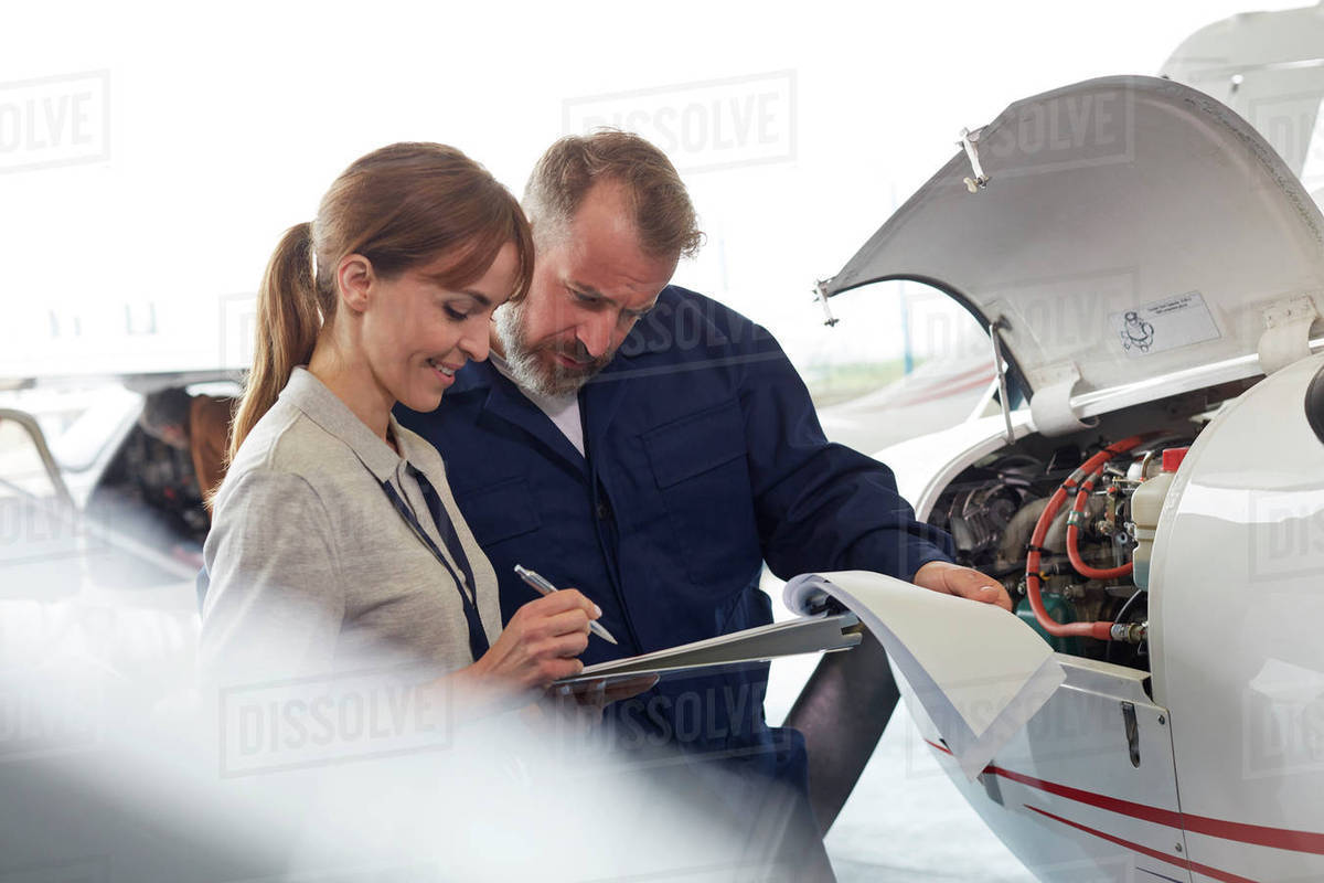 Engineer mechanics reviewing paperwork next to airplane in hangar ...