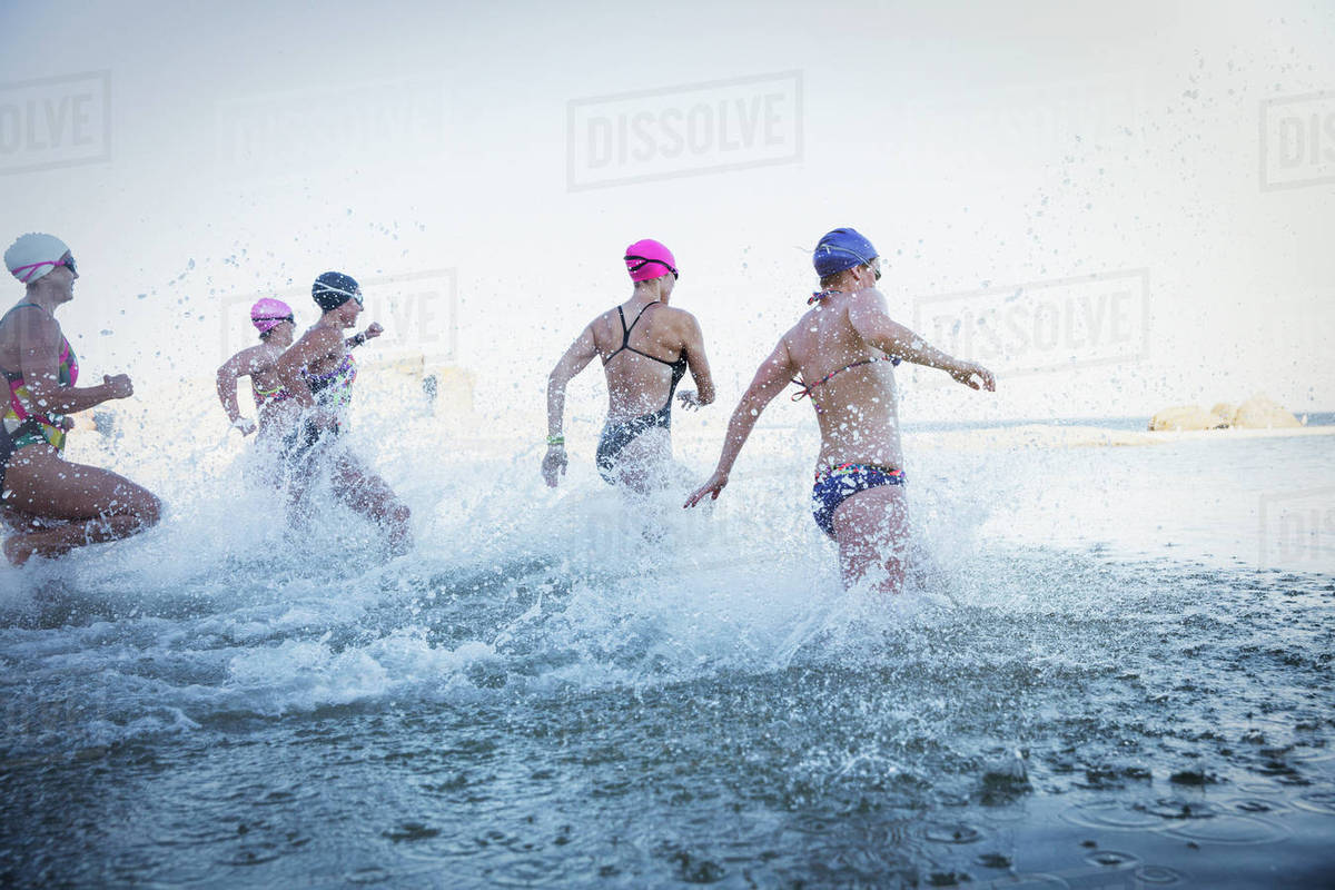 Female open water swimmers running and splashing in ocean surf ...