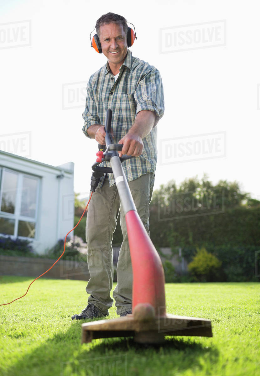 Man using weed whacker in backyard - Royalty-free Stock Photo | Dissolve