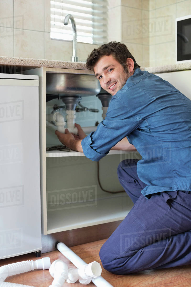 Plumber working on pipes under kitchen sink - Stock Photo - Dissolve