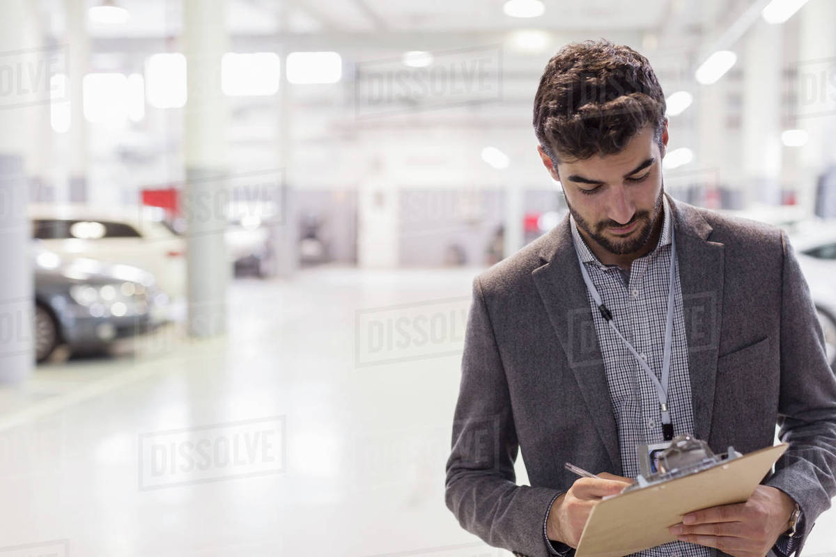 Car salesman writing on clipboard in car dealership auto repair shop ...