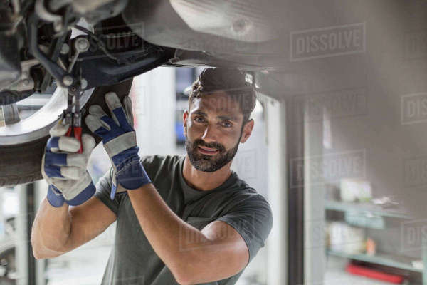 Portrait confident male auto mechanic working under car in auto repair ...