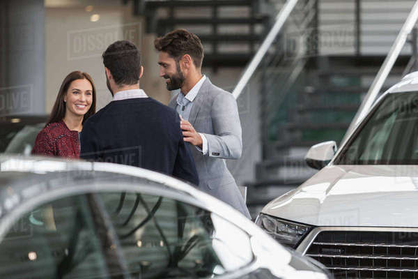 Car salesmen talking to female customer in car dealership showroom ...