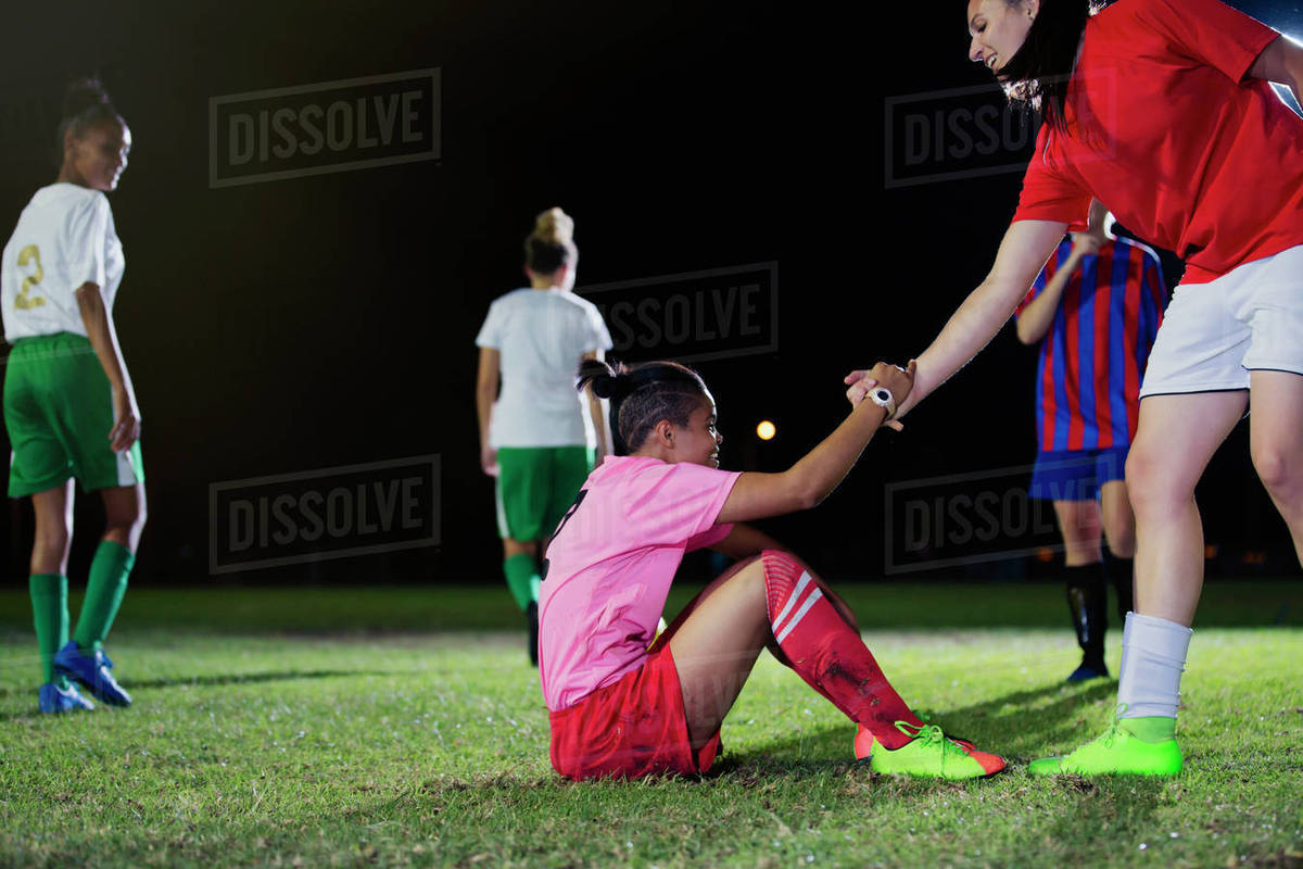 Young female soccer player helping fallen teammate get up on field at ...