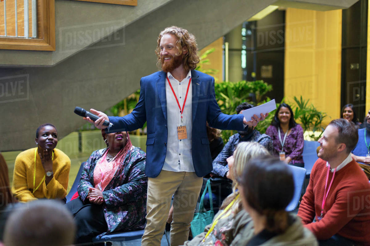 Smiling male speaker with microphone talking to conference audience ...