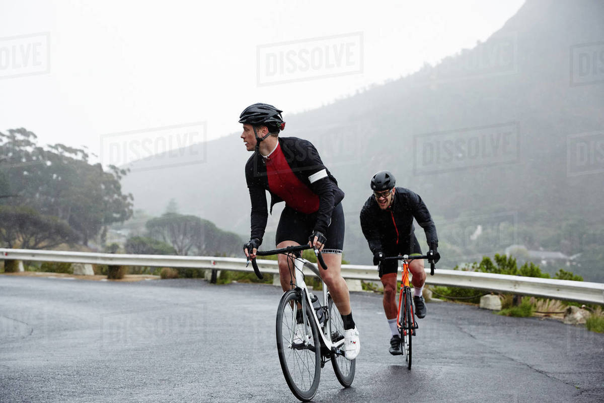 Dedicated male cyclists cycling on wet road - Stock Photo - Dissolve