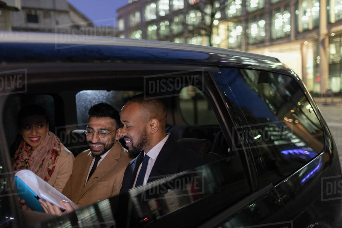 Business people reviewing paperwork in crowdsourced taxi at night ...