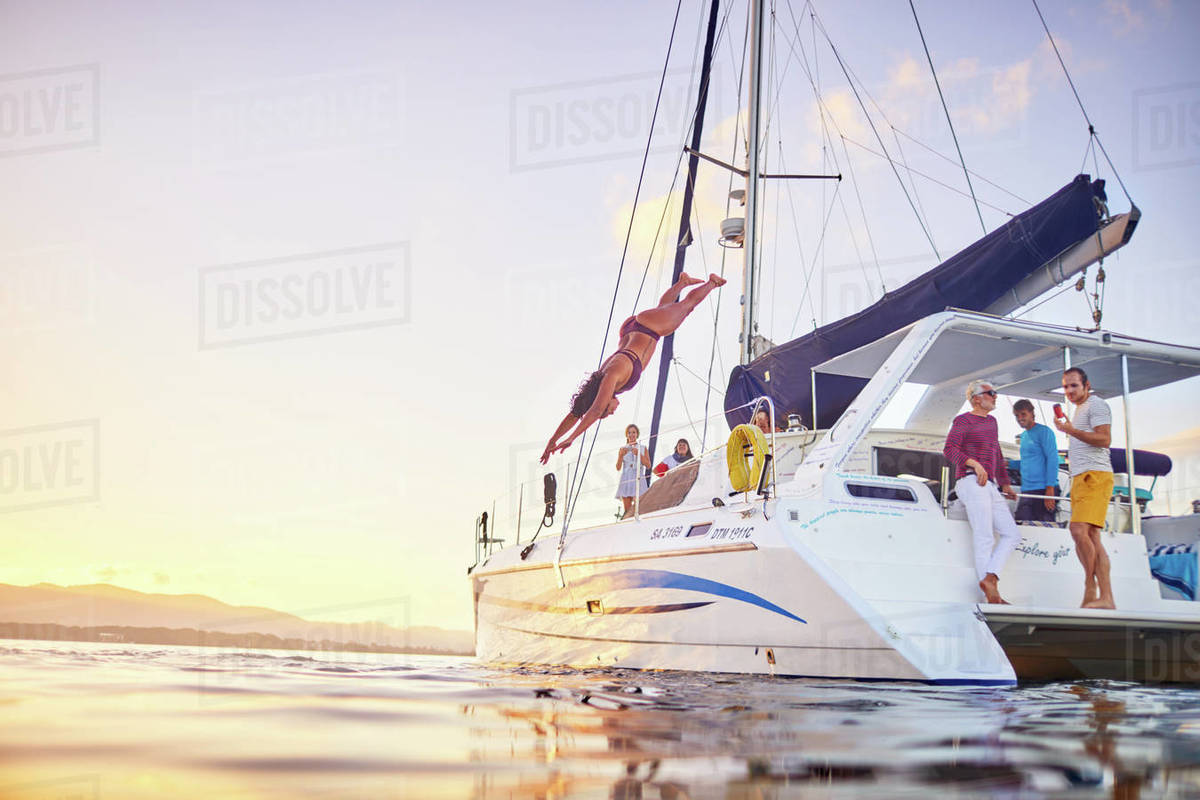 Young woman diving off catamaran into ocean - Stock Photo - Dissolve