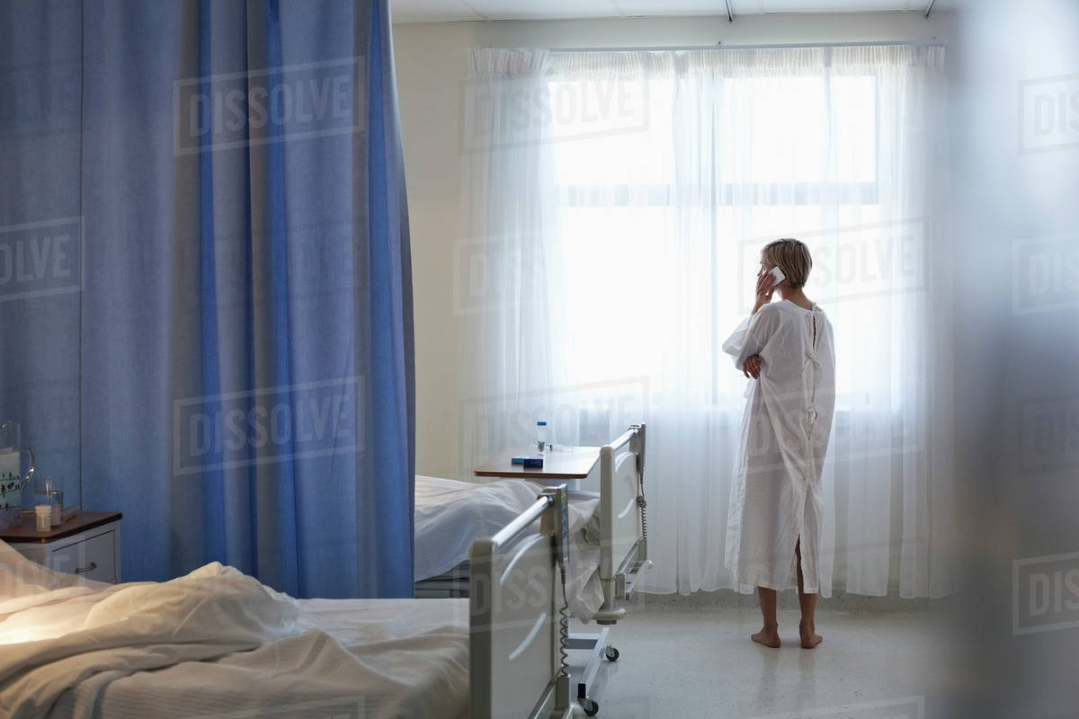 Patient in gown talking on cell phone in hospital room - Royalty-free ...