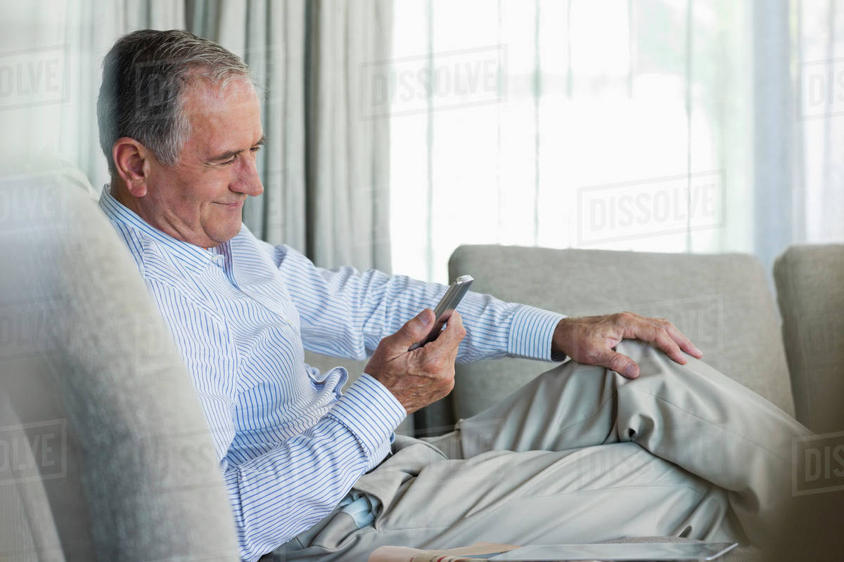 Older man using cell phone on sofa - Stock Photo - Dissolve