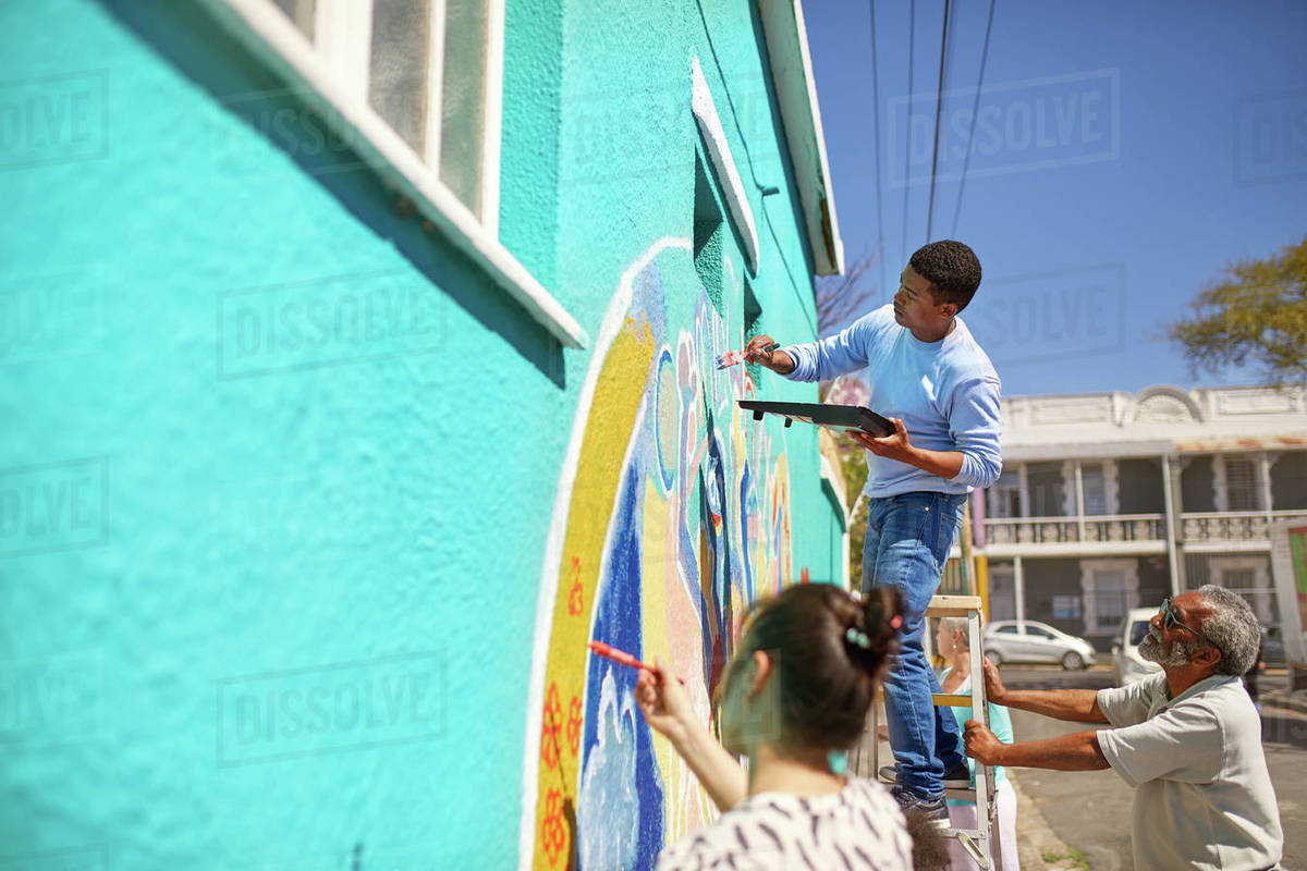 Community volunteers painting vibrant mural on sunny urban wall - Stock ...
