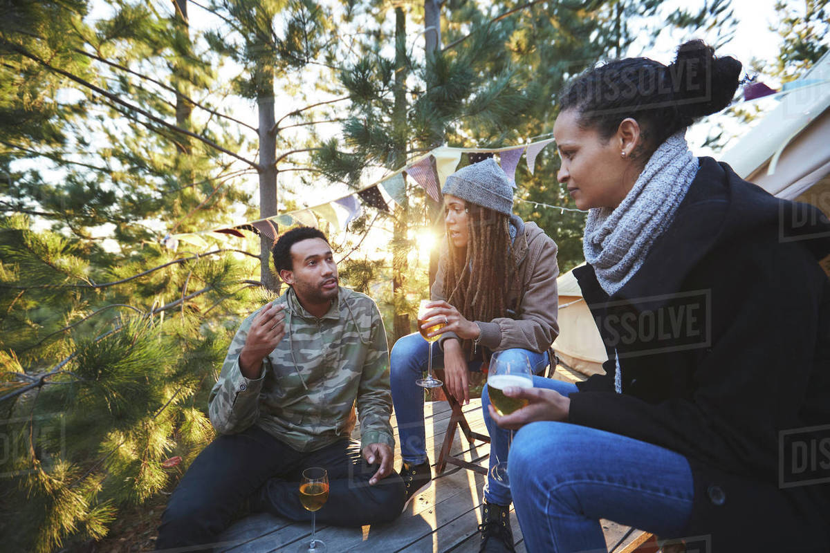 Friends drinking wine and talking at sunny campsite in woods - Stock ...
