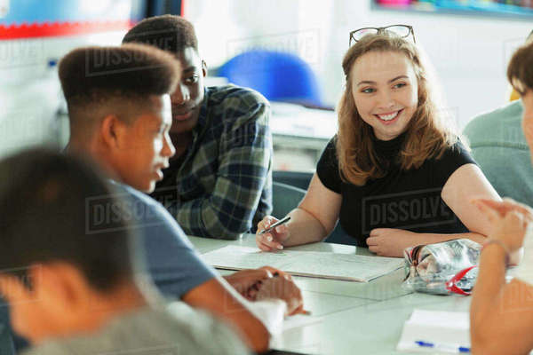Smiling high school girl student talking with classmates in classroom ...