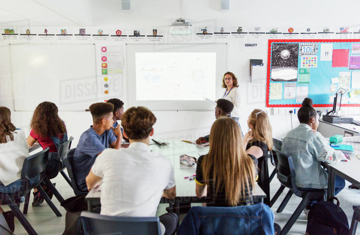 High school students watching female teacher leading lesson at ...