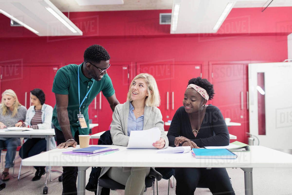 Community college instructor helping students with paperwork in ...
