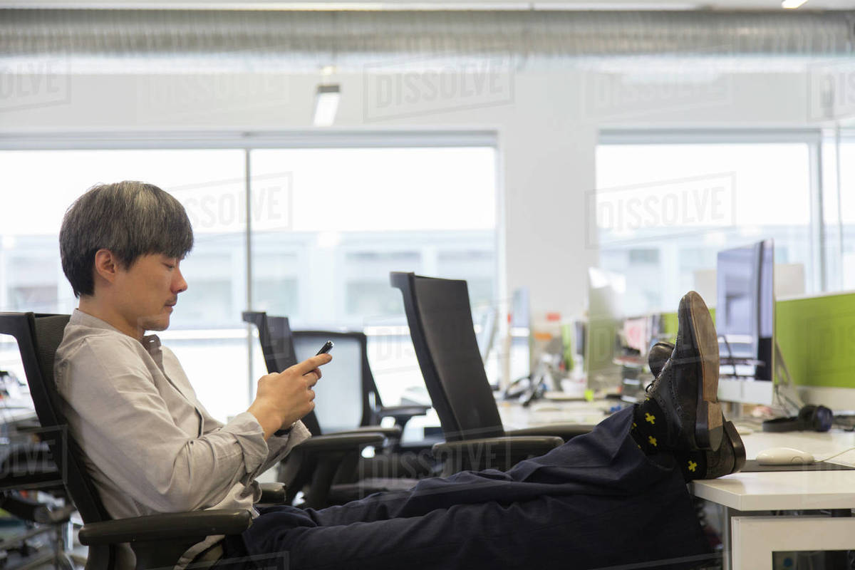 Businessman using smart phone with feet up on office desk - Royalty ...