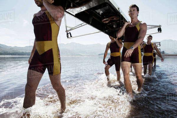 Rowing team carrying scull out of lake - Stock Photo - Dissolve