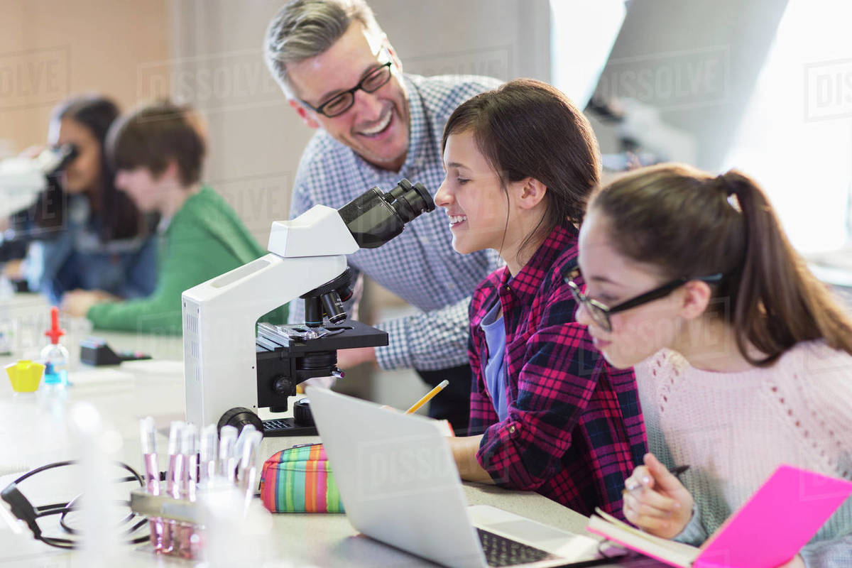 Smiling male science teacher helping girl students conducting ...