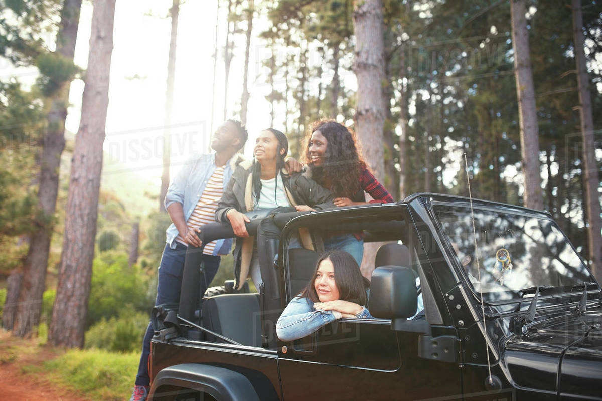 Young friends in jeep looking up at trees in woods, enjoying road trip ...