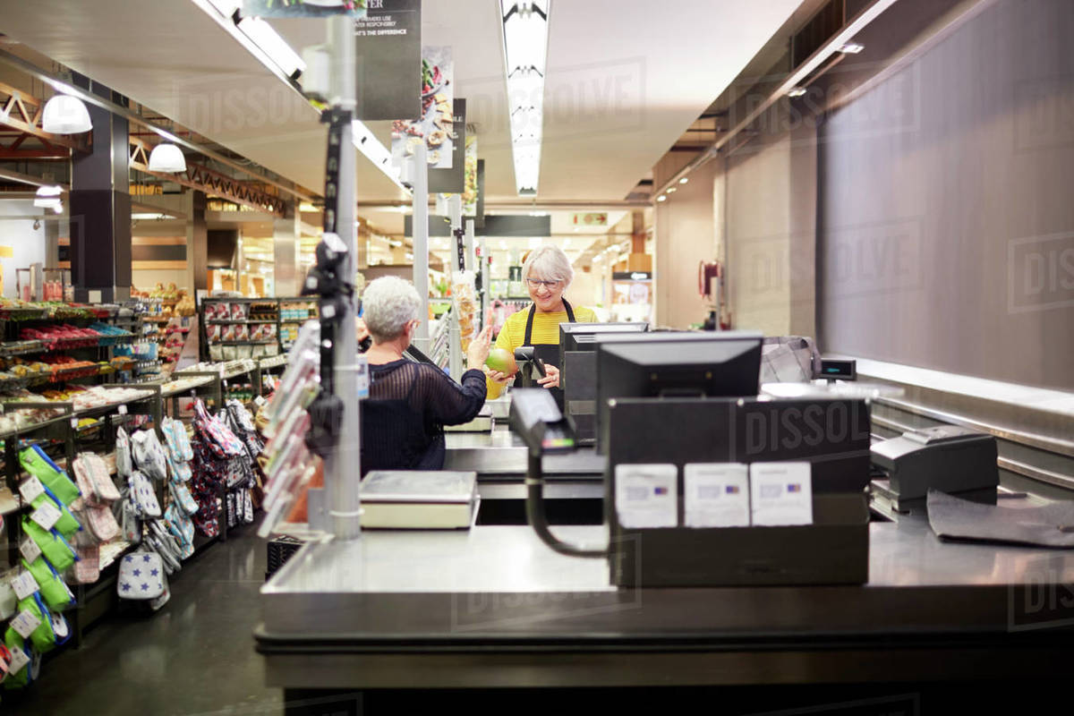 Senior female cashier helping customer at supermarket checkout ...