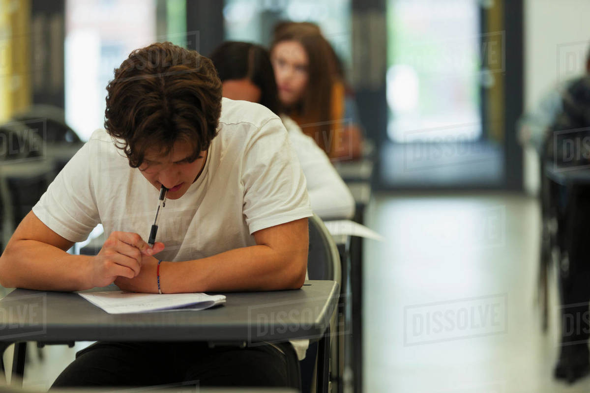 Focused high school boy student taking exam at desk in classroom ...