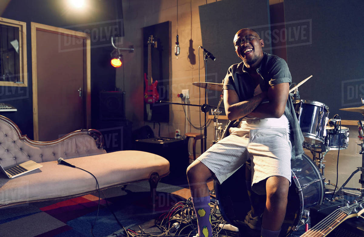 Portrait happy male musician sitting on drums in recording studio ...