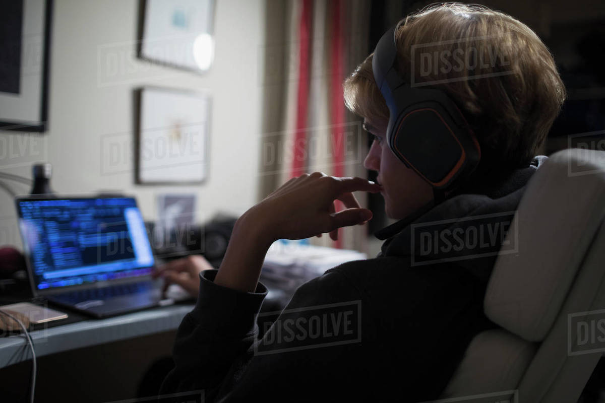Teenage boy with headphones using computer in dark bedroom - Royalty ...